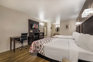 Quarto de hotel com cama, escrivaninha, cadeira, televisão e um pequeno frigorífico.