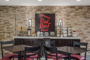 Área de café da manhã do Red Roof Inn, com parede de pedra ao fundo, máquina de café, dispensadores de cereais e torradeira.