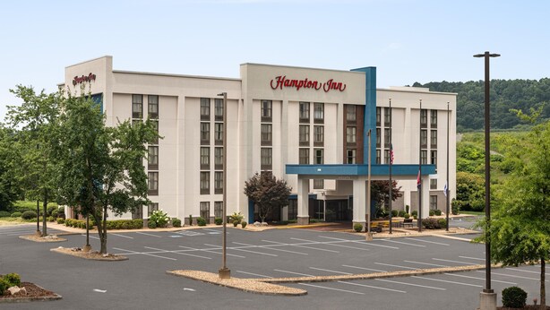 Hotel Hampton Inn com fachada moderna, estacionamento e área verde ao redor.