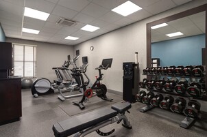 Academia com equipamentos de ginástica, um banco e uma barra de halteres.