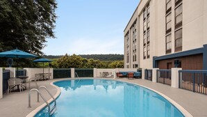 Piscina com escada de metal, rodeada por mobiliário de exterior e guarda-sóis.
