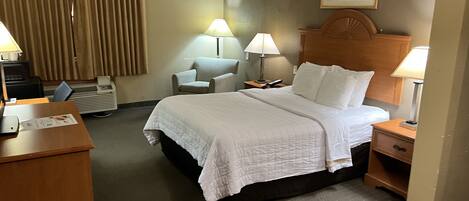 Quarto de hotel com uma cama grande, duas mesas de cabeceira com abajures, uma cadeira, uma escrivaninha e uma TV fixada na parede.