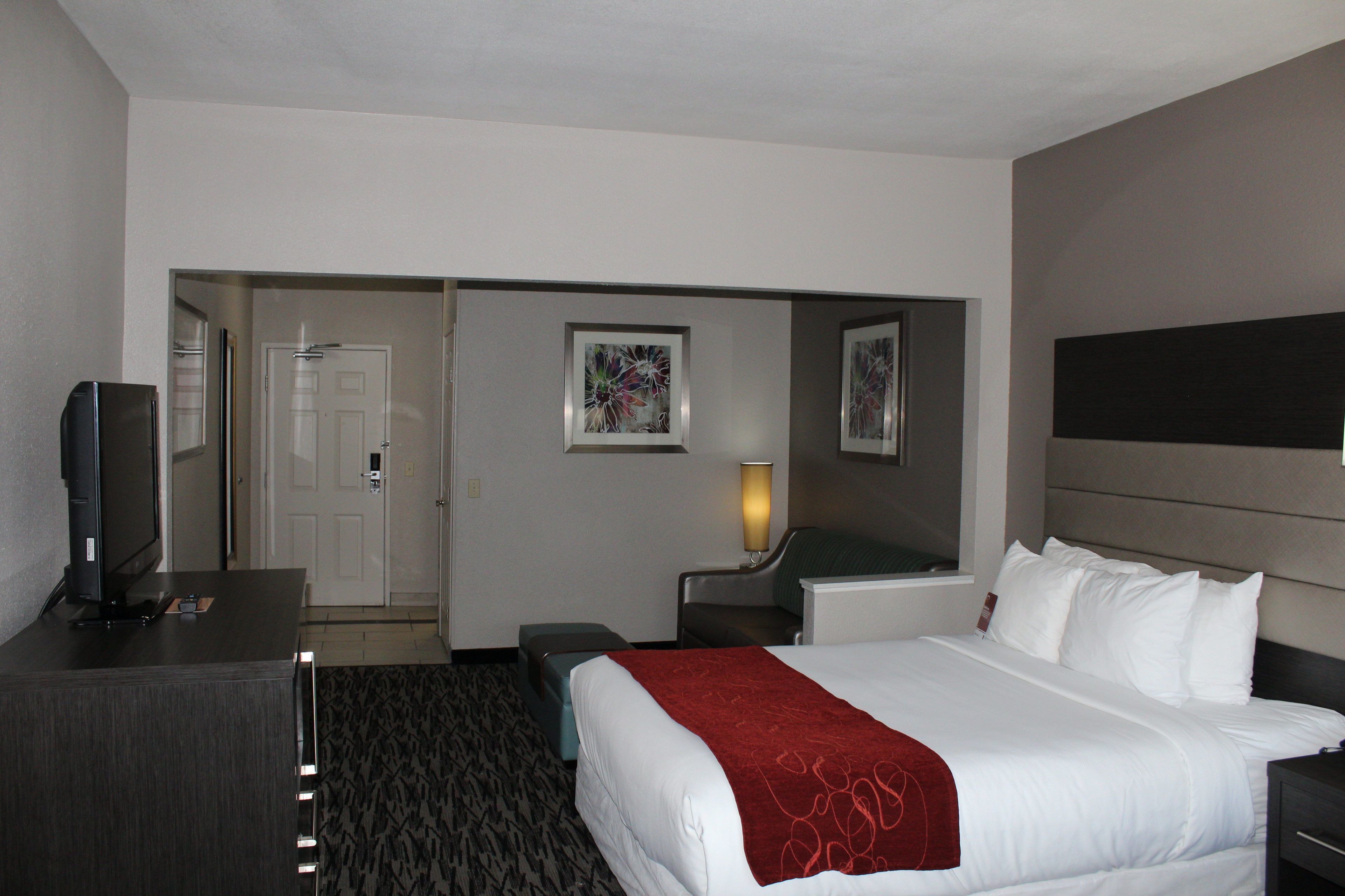 Quarto de hotel com cama, escrivaninha, televisão e porta que dá para outro aposento.