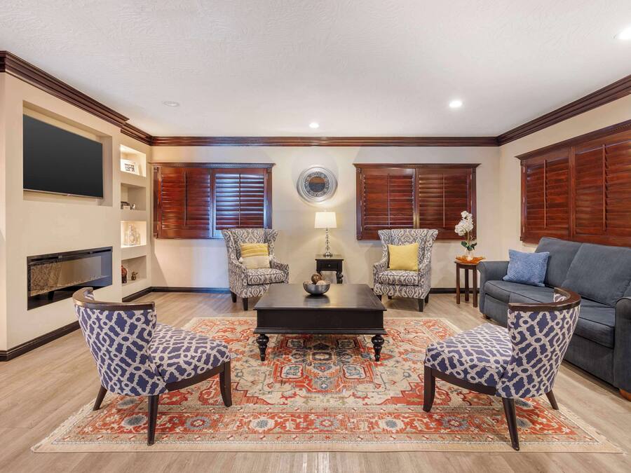 Uma sala de estar com lareira, duas poltronas estampadas, um sofá, uma mesa de centro e um tapete decorativo.
