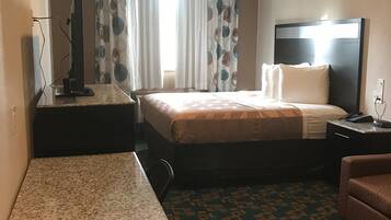 Quarto de hotel com cama, escrivaninha, cadeira, televisão e mesa de cabeceira.