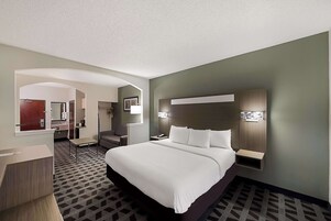 Quarto de hotel com uma cama grande, uma escrivaninha, uma cadeira, uma mesa de cabeceira e uma luminária fixa na parede.