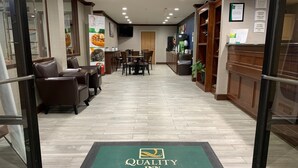 Um saguão de hotel com balcão de recepção, área de estar e um tapete verde com o nome do hotel.