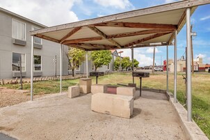 Uma área de estar coberta ao ar livre, com bancos de concreto e estrutura metálica no telhado.