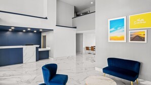 Um lobby moderno com piso de mármore, balcão de recepção, assentos azuis e obras de arte emolduradas.