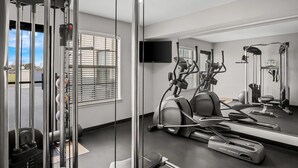 Uma academia com equipamentos de ginástica, um espelho grande e uma televisão na parede.