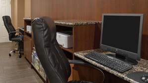 Um escritório de hotel com uma cadeira de couro, um computador de mesa e uma impressora sobre uma escrivaninha de madeira.
