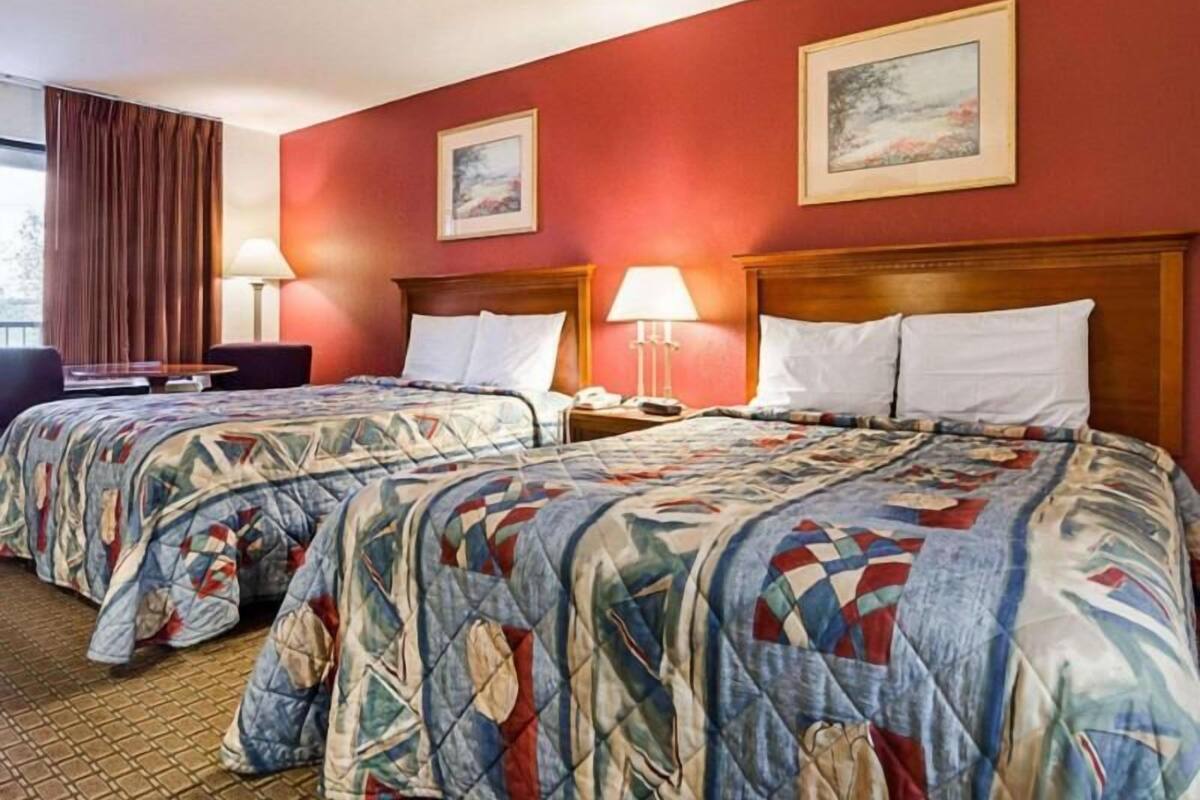 Quarto de hotel com duas camas, uma mesa, uma cadeira e uma janela com cortinas.
