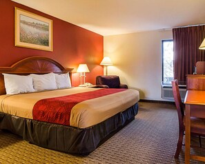 Quarto de hotel com uma cama grande, duas luminárias de cabeceira, uma cadeira, uma escrivaninha e uma janela com cortinas.