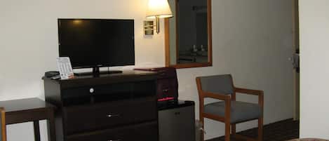 Quarto de hotel com cama, escrivaninha com televisão, cadeira, cómoda e espelho.