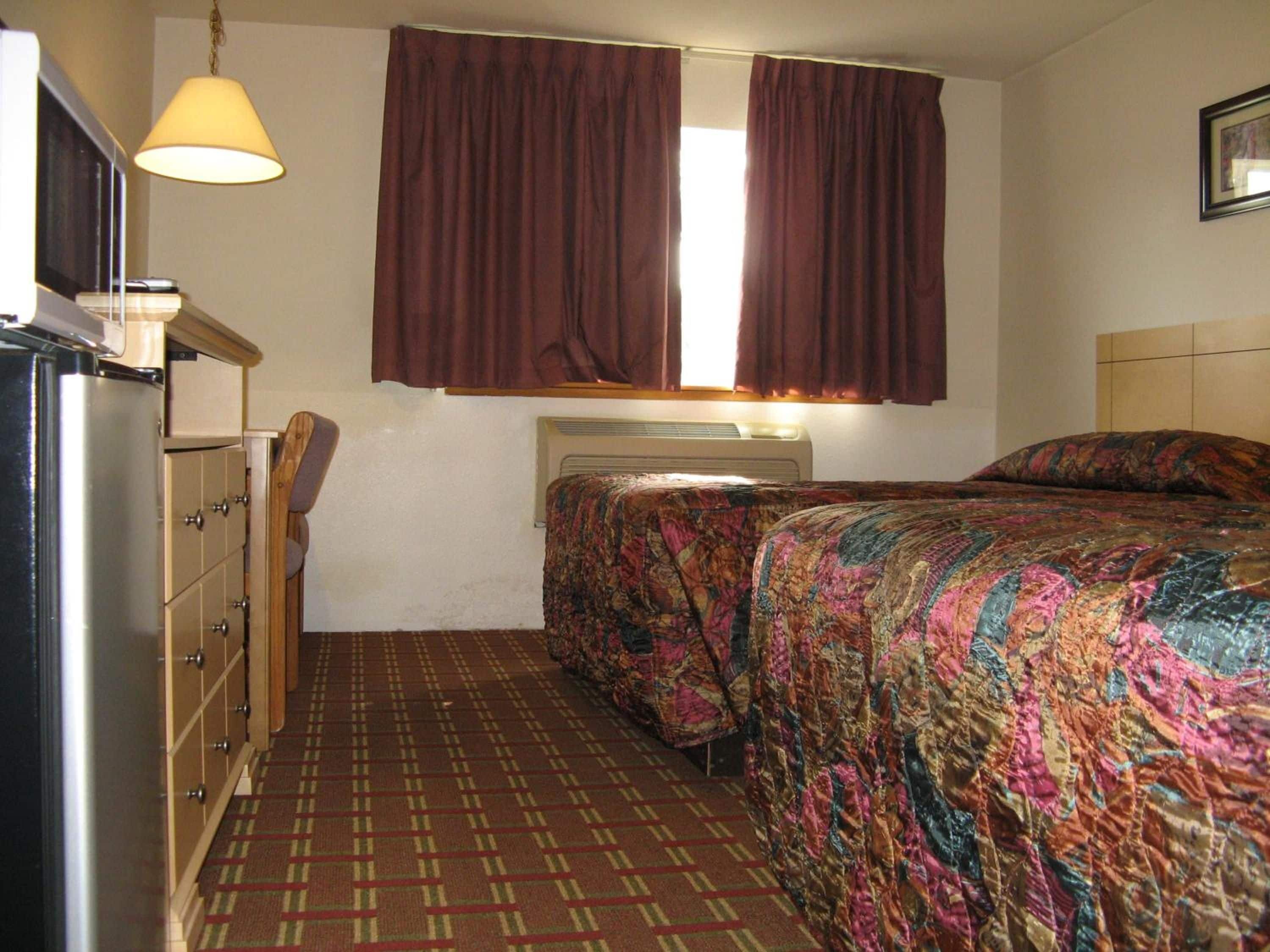Um quarto pequeno com uma cama, cômoda, janela com cortinas e radiador.