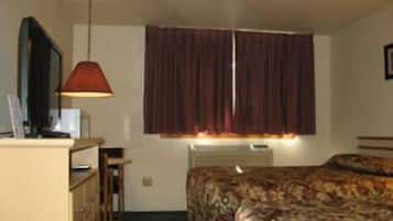 Um quarto pequeno e modesto, com uma cama, uma escrivaninha, uma cadeira e uma televisão.