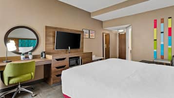 Quarto de hotel com cama, escrivaninha com computador, televisão, espelho e micro-ondas.