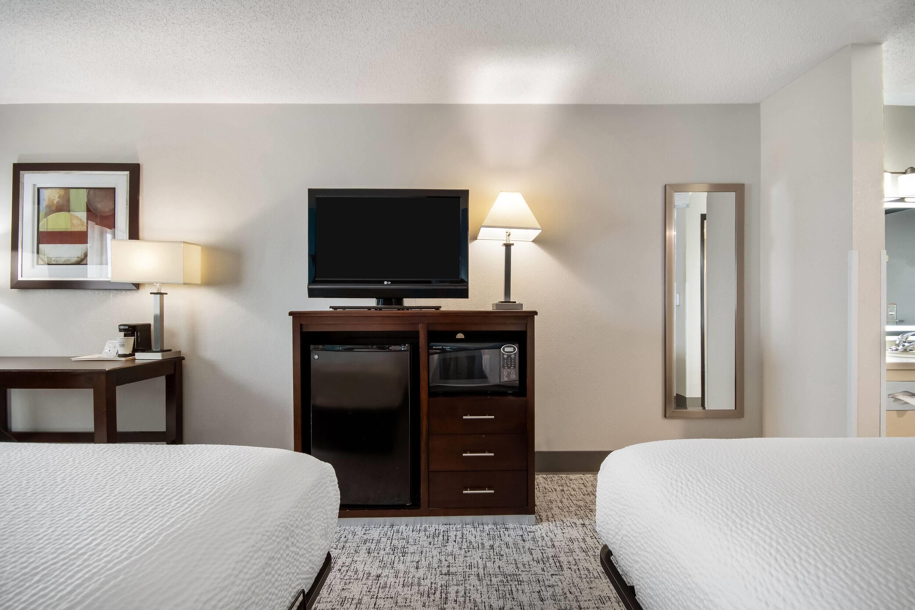 Quarto de hotel com duas camas, televisão de tela plana, micro-ondas, máquina de café e uma luminária.