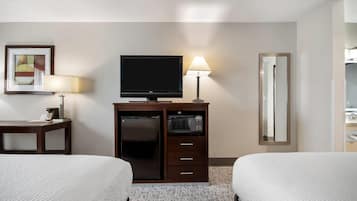 Quarto de hotel com duas camas, televisão de tela plana, micro-ondas, máquina de café e uma luminária.