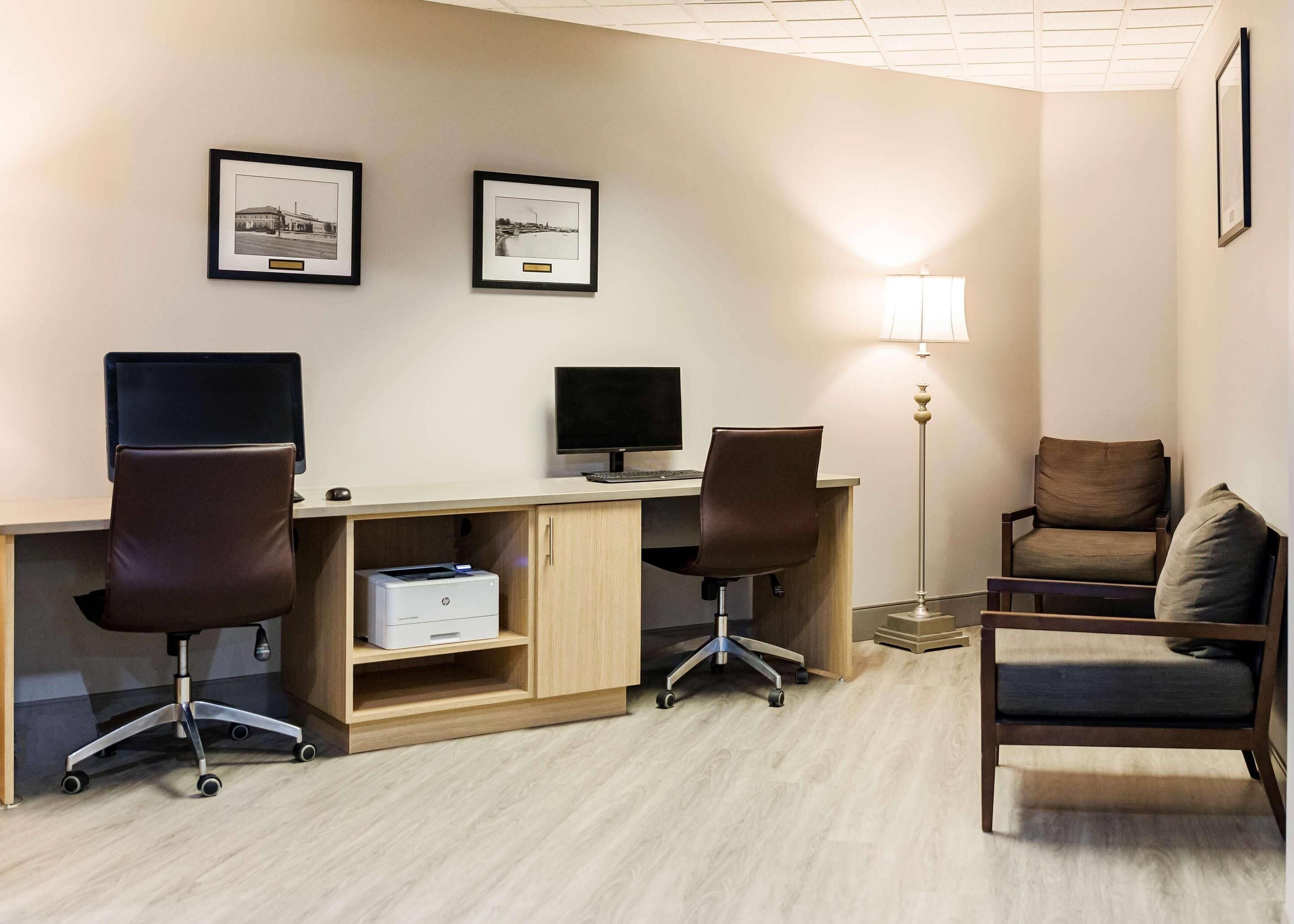 Quarto de hotel com escrivaninha, duas cadeiras, computador, impressora e luminária.