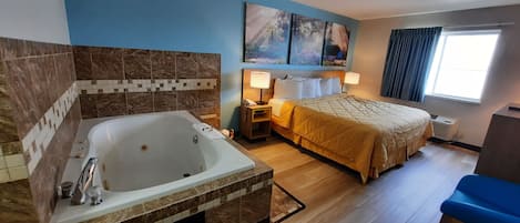 Quarto de hotel com uma banheira grande, uma cama com cobertura acolchoada, uma mesa de cabeceira com abajur e um quadro sobre a cama.