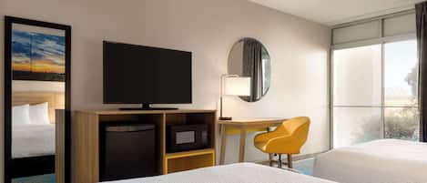 Quarto de hotel com duas camas, televisão, escrivaninha com cadeira, micro-ondas e uma janela grande.
