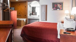 Quarto de hotel com uma cama grande, uma escrivaninha, uma cômoda, uma toucador com espelho e um quadro na parede.