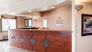 Uma receção com acabamento em madeira e padrões de diamantes decorativos, uma placa na parede com a inscrição "Quality by Choice Hotels" e uma moldura com um quadro na parede.