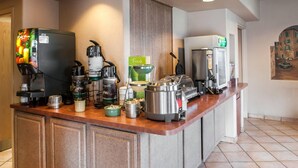 Uma cozinha de hotel com um espaço para café, um dispensador de suco fresco e diversos eletrodomésticos de cozinha.