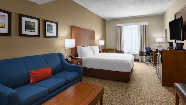 Quarto de hotel com uma cama grande, um sofá azul, uma mesa de centro de madeira, uma escrivaninha com um computador e uma televisão.