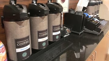 Uma estação de café com três dosadores de café identificados como 'Premium Select Coffee Medium' e um cesto de cápsulas de café.