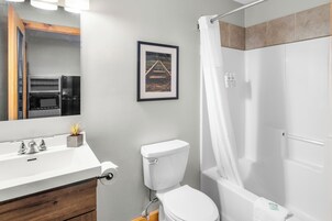 Casa de banho com lavatório branco, sanita e chuveiro com cortina.