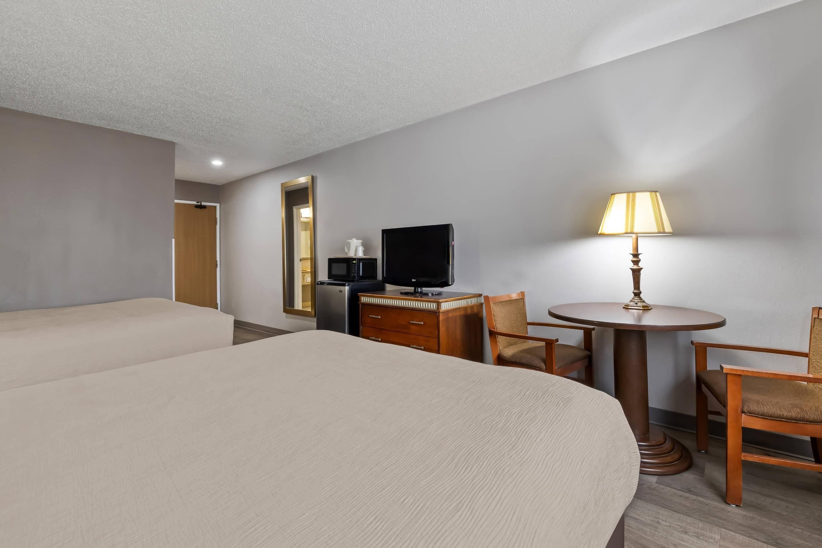 Quarto de hotel com duas camas, uma escrivaninha com televisão, uma luminária e uma cadeira.