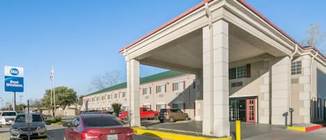 Um hotel Best Western com área de estacionamento coberta, um carro vermelho e um céu azul límpido.