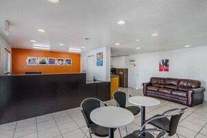 Uma área de recepção com balcão, um sofá de couro marrom e duas mesas redondas com cadeiras.