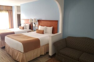 Quarto de hotel com duas camas, um sofá e uma janela grande com cortinas.