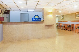 Uma área de recepção com o letreiro Days Inn, um balcão de atendimento e várias cadeiras de madeira dispostas para os hóspedes.