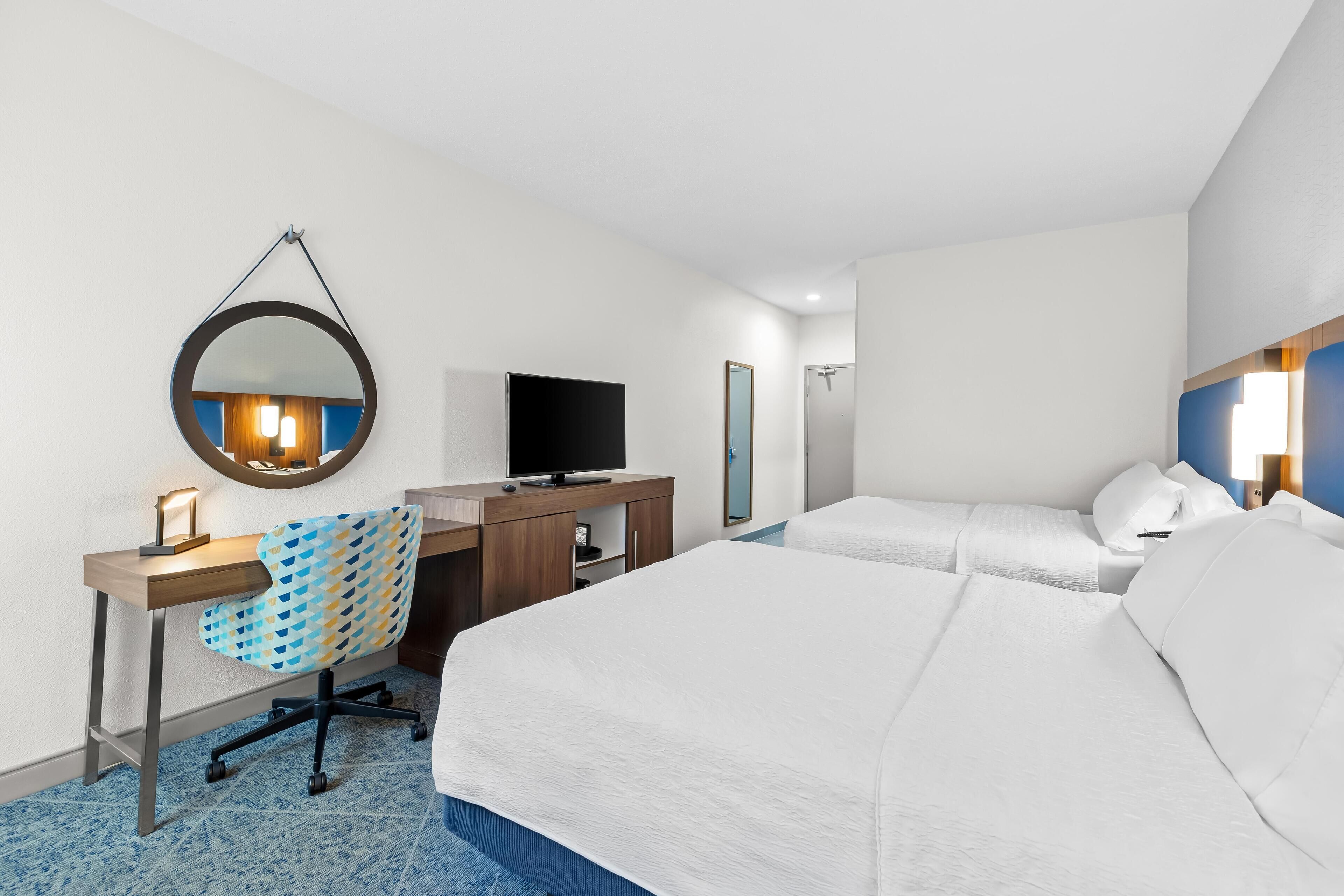 Quarto de hotel com uma cama grande, uma escrivaninha com cadeira, televisão e espelho.