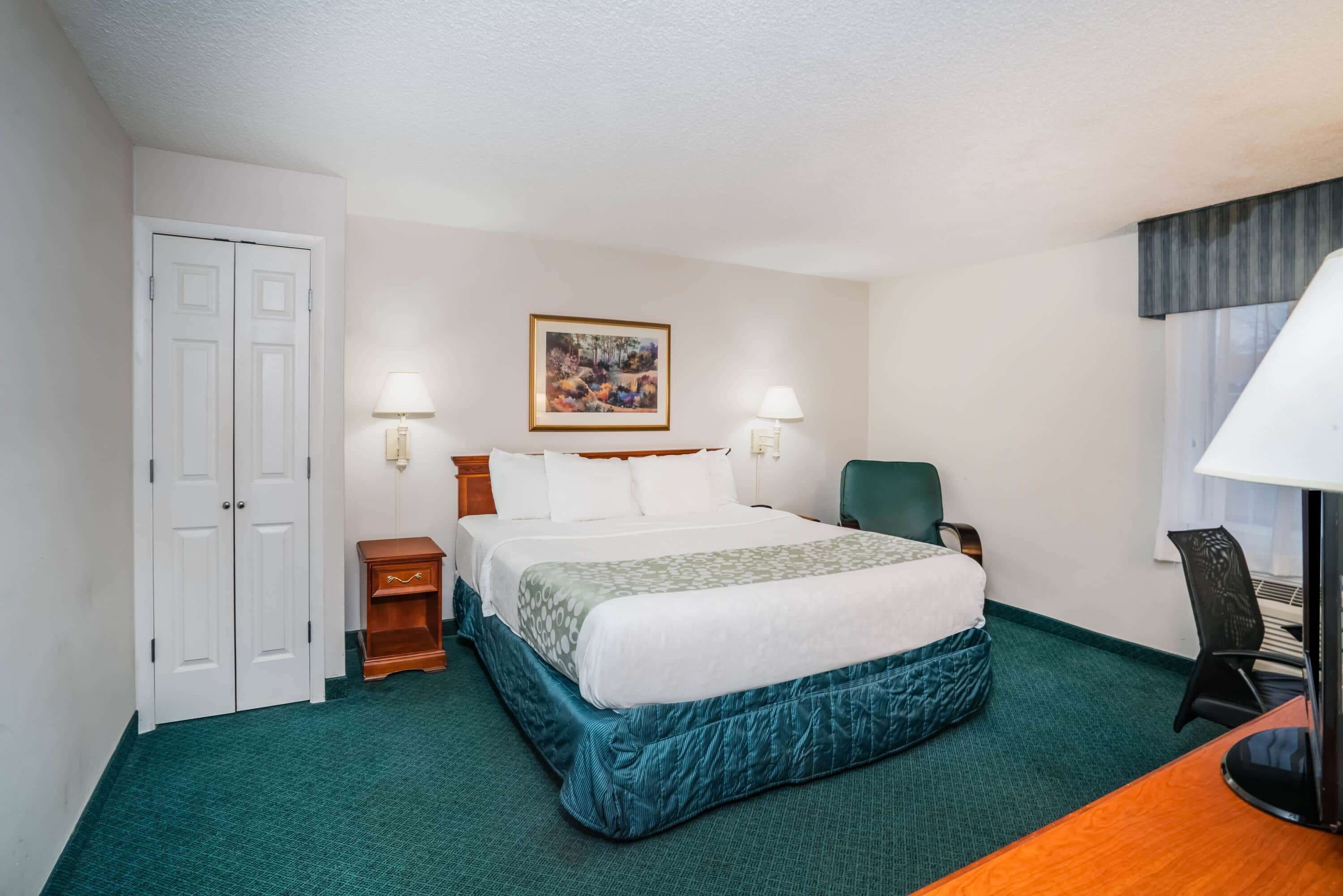 Quarto de hotel com cama, duas mesas de cabeceira, escrivaninha, cadeira, abajur e um quadro na parede.