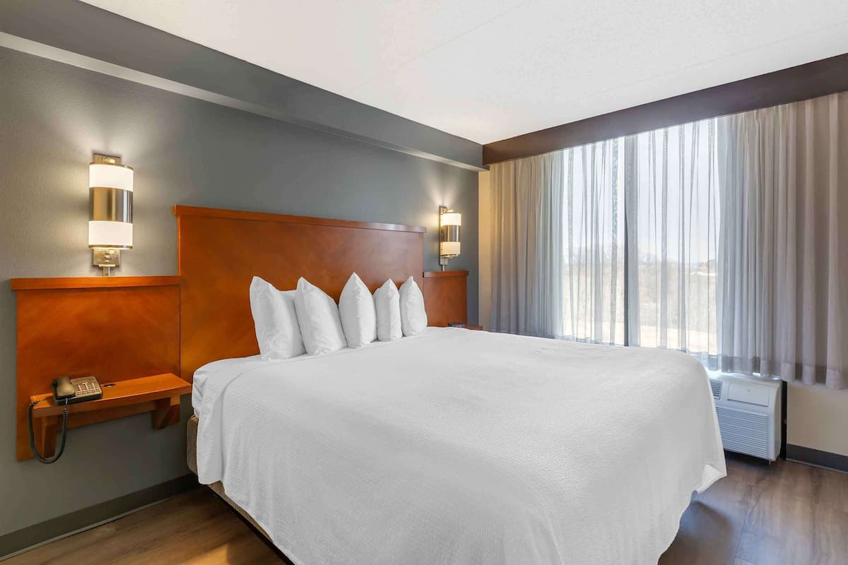 Quarto de hotel com uma cama grande, duas mesas de cabeceira com luminárias, um telefone e uma janela com cortinas.