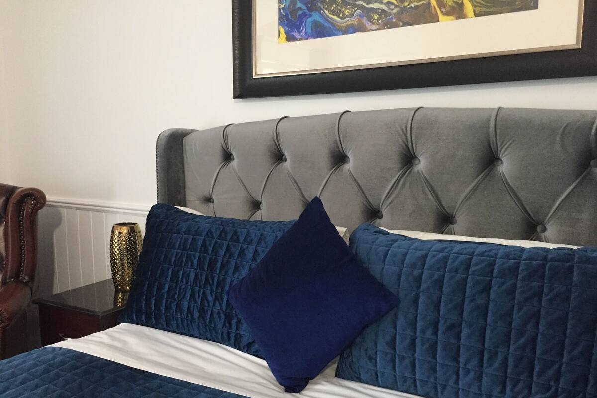 Uma cama com cabeceira estofada, colcha matelada azul e duas almofadas azuis.