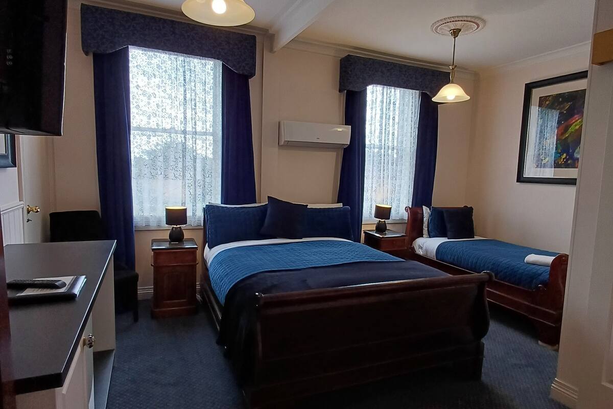 Quarto de hotel com duas camas, uma escrivaninha, uma televisão e um ventilador de teto.