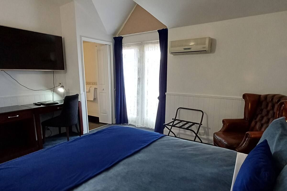 Quarto de hotel com uma cama, uma escrivaninha com cadeira, televisão e aparelho de ar condicionado.