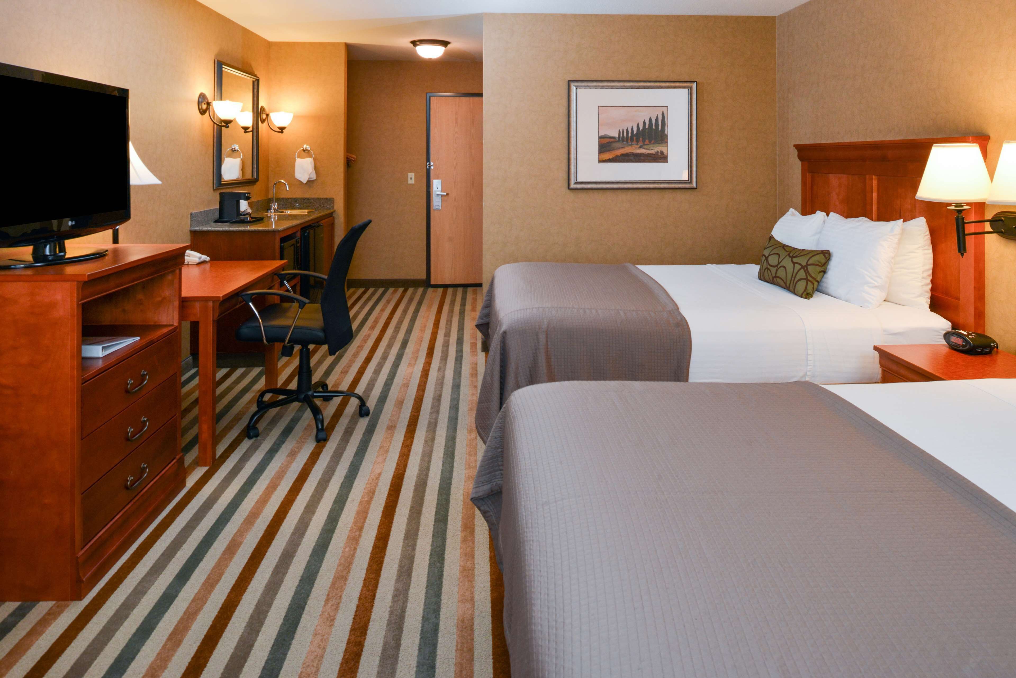 Quarto de hotel com duas camas, uma escrivaninha com cadeira, televisão e casa de banho visível através de uma porta aberta.