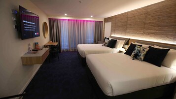 Quarto de hotel com duas camas, uma escrivaninha, televisão e vista para a rua através da janela.
