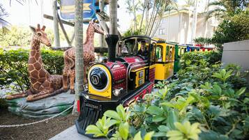 Um trem em miniatura com locomotiva preta e amarela, passando por duas estátuas de girafa.