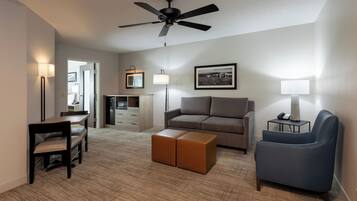 Quarto de hotel com ventoinha no teto, sofá, poltrona, mesa e cadeiras e abajur.