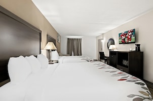 Quarto de hotel com uma cama grande, duas mesas de cabeceira com abajures, uma escrivaninha, uma televisão e um guarda-roupa.