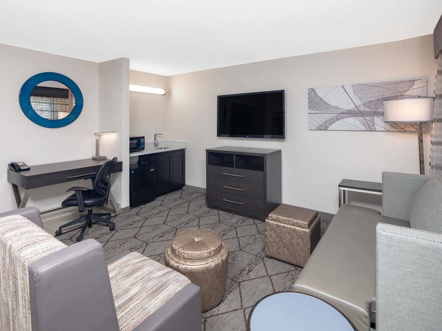 Quarto de hotel com escrivaninha, televisão, sofá e mesa redonda pequena.