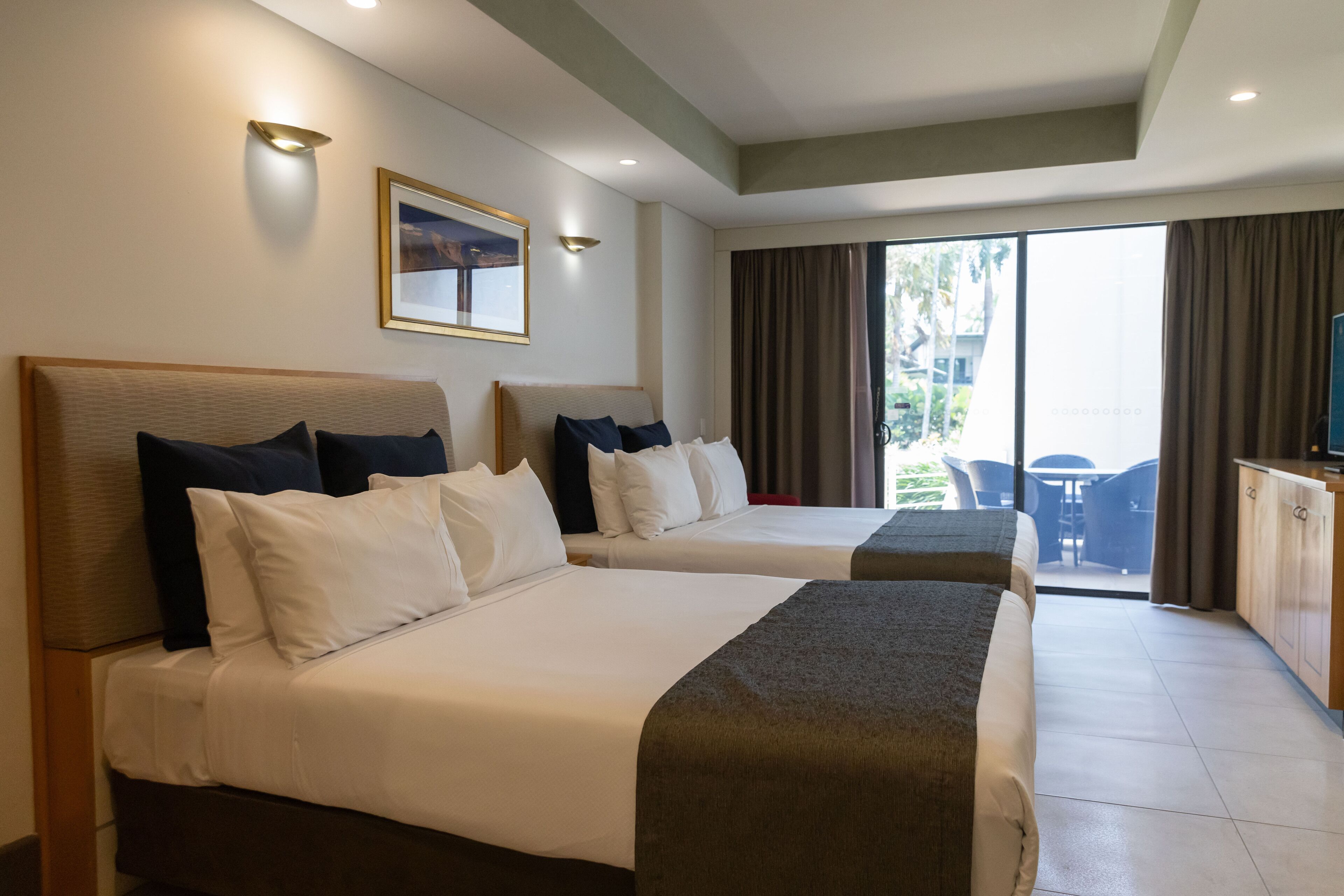 Quarto de hotel com duas camas, televisão, área de refeições e vista para o exterior.